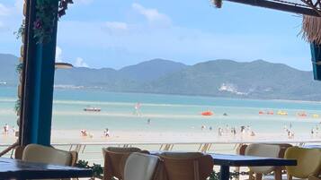 Um restaurante à beira-mar com mesas ao ar livre e vista para a praia e montanhas.