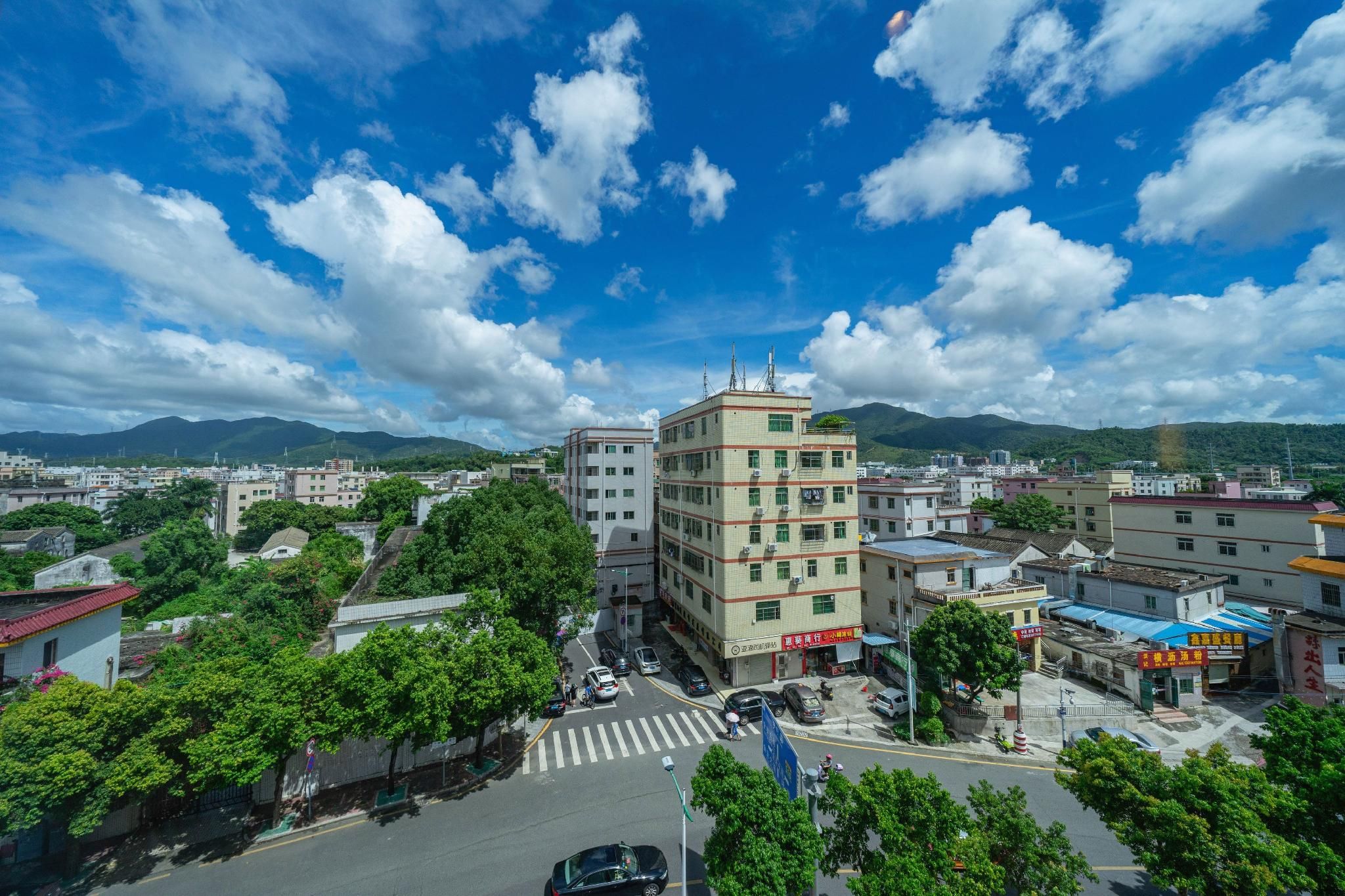 Um edifício de vários andares com telhado plano, cercado por vegetação e outros edifícios.