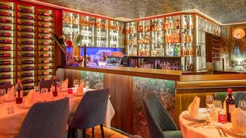 Uma área de bar com prateleiras cheias de garrafas e copos, um relógio e mesas preparadas para refeições.