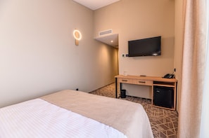 Quarto de hotel com cama, escrivaninha, televisão e pequeno frigorífico.