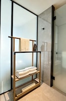 Um banheiro moderno com box de vidro, porta-toalhas de madeira e piso de mármore.