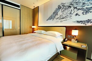 Quarto de hotel com cama, mesa de cabeceira, telefone e painel de controle fixado na parede.