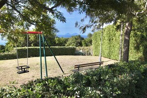 Um parque com baloiço, um banco e vista para o mar.