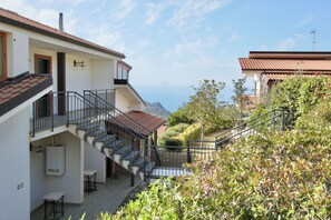Um edifício com vários andares, uma escadaria que leva a uma varanda, vista para o mar e uma área de jardim.