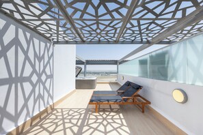 Varanda iluminada pelo sol com teto geométrico, banheira de hidromassagem e uma espreguiçadeira.