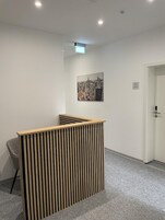 Uma área de recepção com um balcão de madeira ripa, uma pintura da paisagem urbana na parede e uma porta com a identificação '101'.