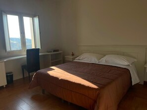 Quarto com cama, cadeira, escrivaninha e janela.