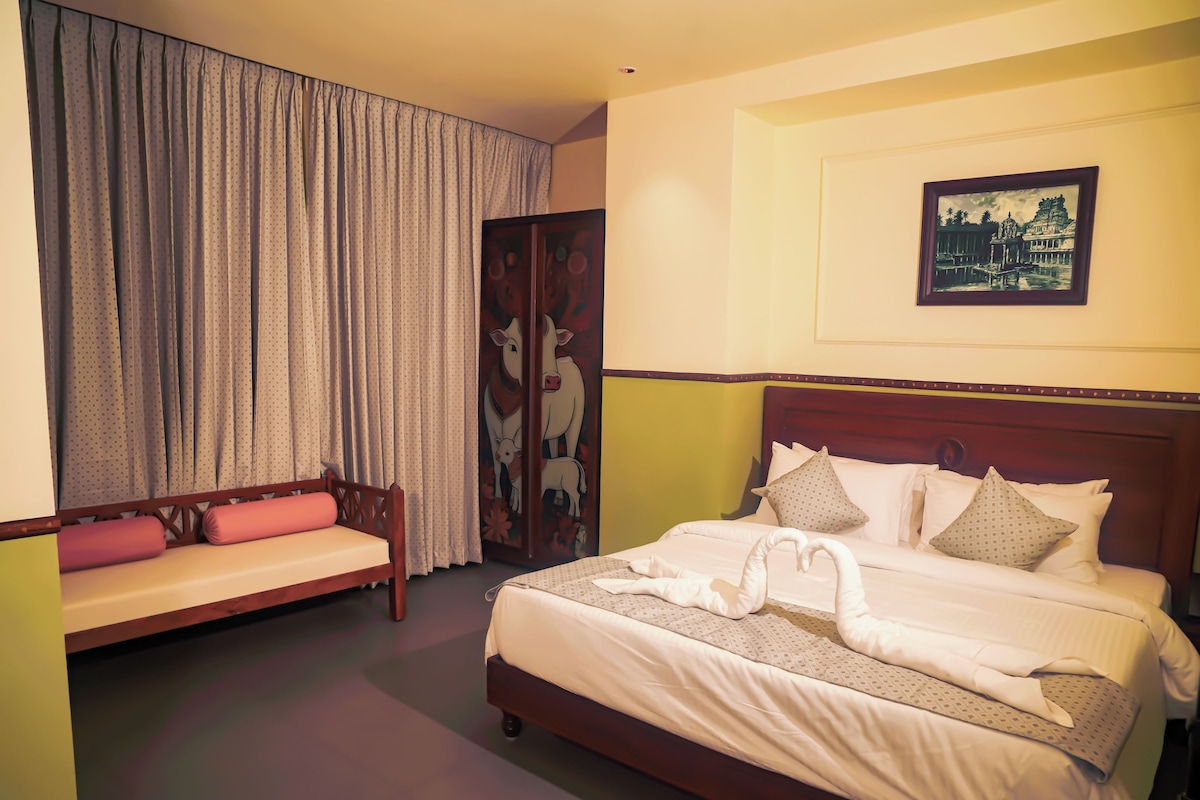 Quarto de hotel com cama, sofá, janela grande com cortinas e quadro na parede.