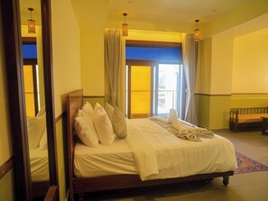 Quarto de hotel com cama grande, espelho, um banco e vista para o exterior.