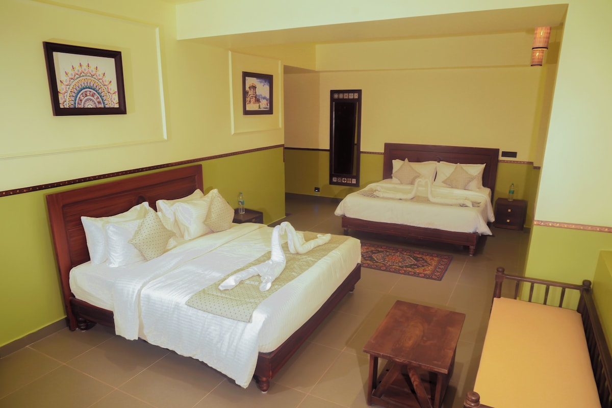Quarto de hotel com duas camas, cabeceira de madeira, uma mesinha e uma cadeira.