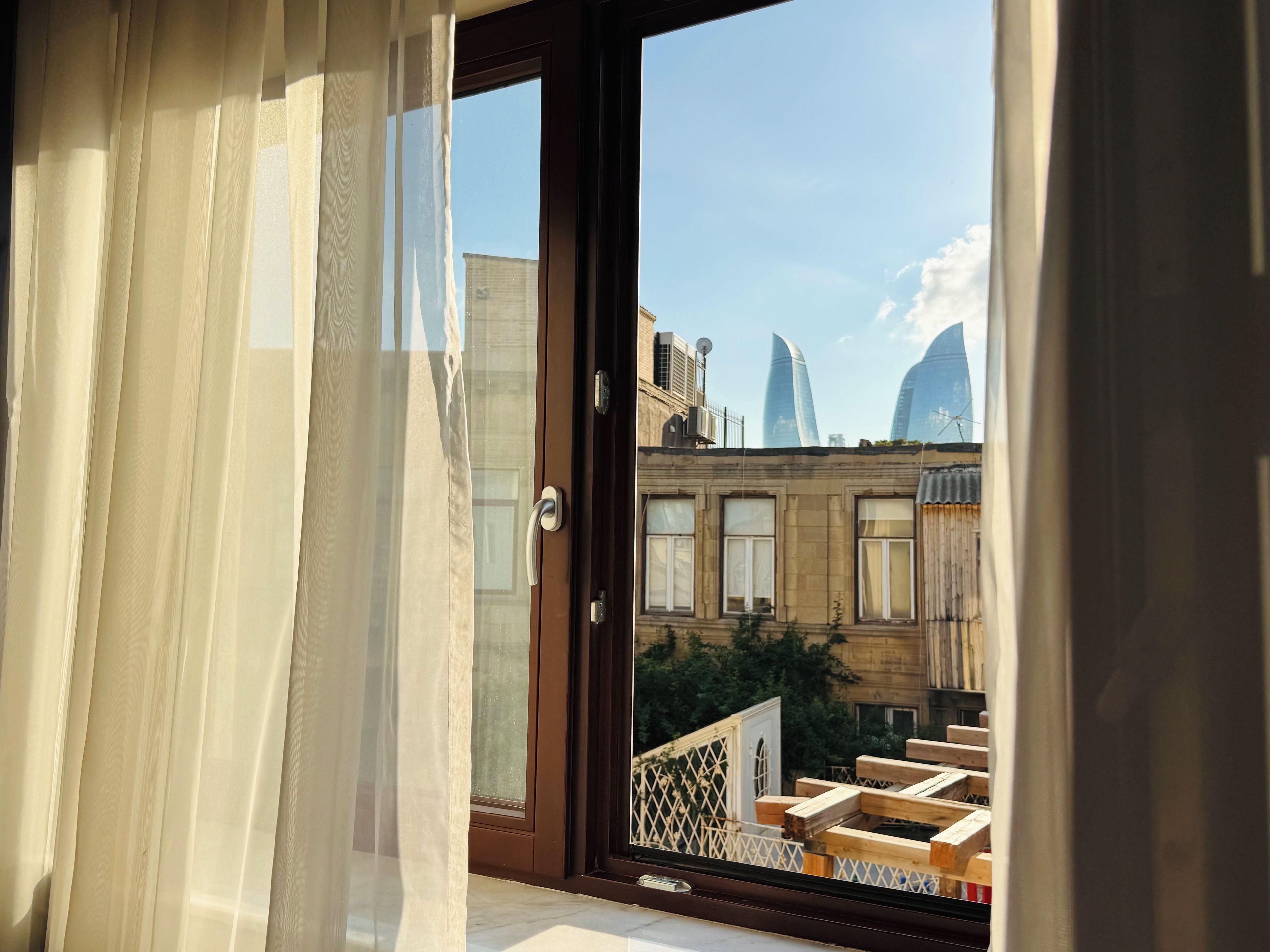 Vista de varanda com porta e cortinas, com vista para um horizonte urbano repleto de edifícios sob um céu limpo.