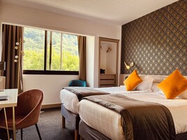 Quarto de hotel com duas camas, uma escrivaninha, uma cadeira e uma janela grande com vista para árvores.