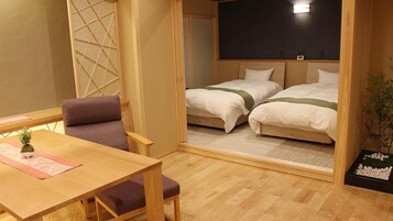 Quarto com mesa de madeira, duas camas, uma pequena planta e uma porta deslizante.