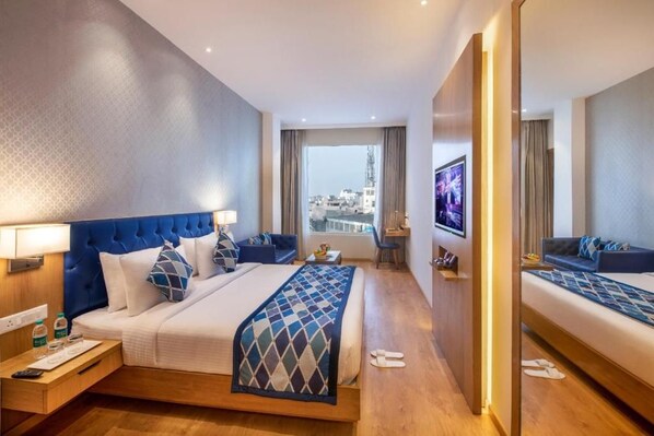 Quarto de hotel com cama grande, escrivaninha, cadeira, televisão e vista para a cidade.