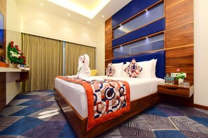 Quarto de hotel com uma cama grande, cabeceira de madeira, mesa de cabeceira com relógio e uma planta decorativa.