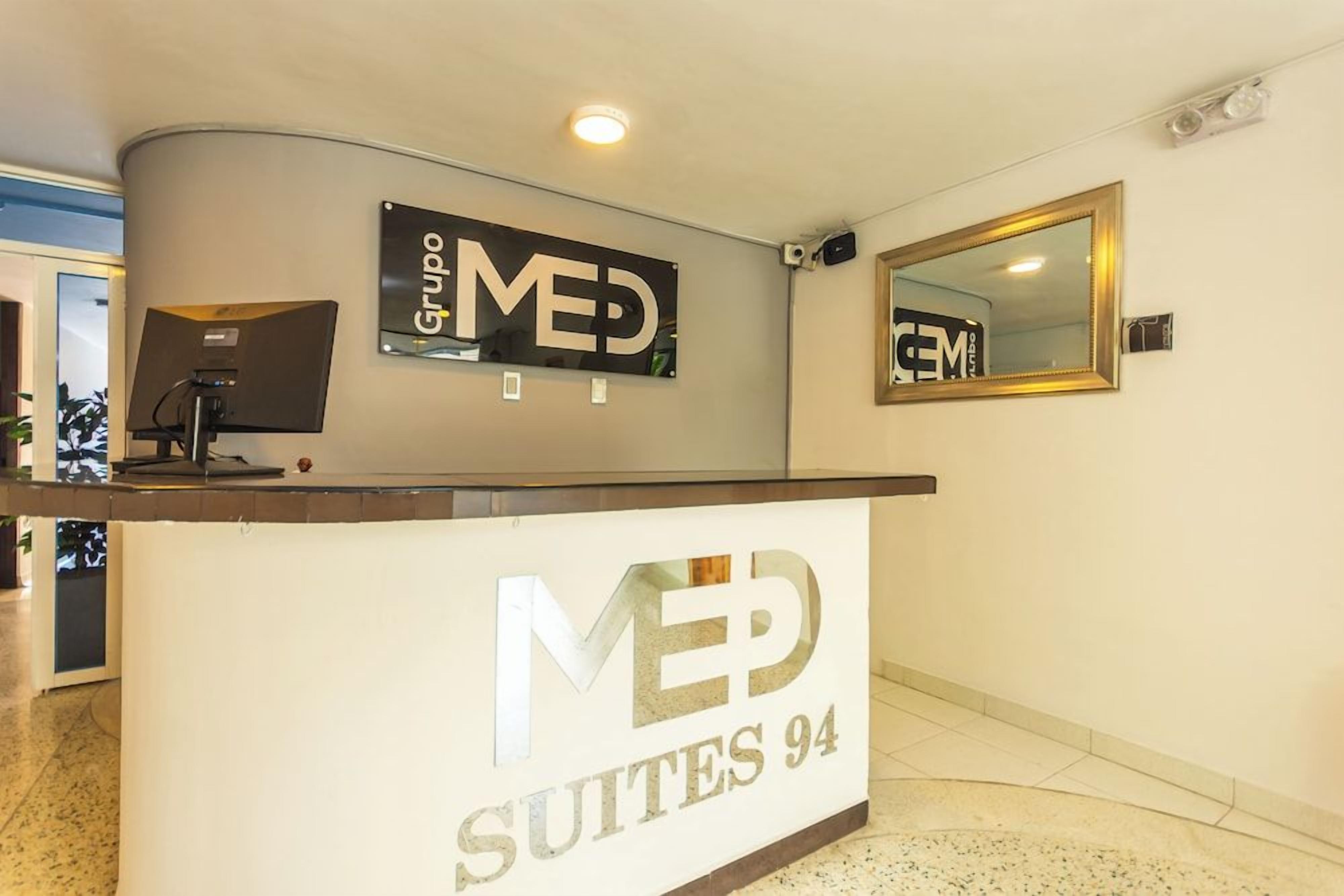 Uma mesa de recepção com a placa 'MED SUITES 94' e um monitor acima.