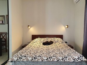 Uma cama de solteiro com colcha estampada, duas luminárias fixadas na parede, cabeceira de madeira e uma tomada na parede.