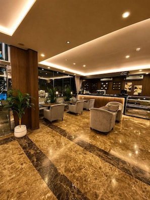 Um hall de hotel com piso de mármore, áreas de estar, balcão de recepção e uma mesa de sobremesas.