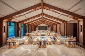 Uma sala de conferência com várias mesas redondas, cada uma delas rodeada por cadeiras com fitas azuis, preparada para uma reunião ou evento.