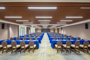 Sala de conferências com fileiras de mesas e cadeiras, equipada com iluminação pendente.