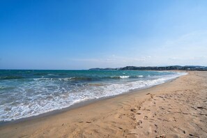 Uma praia com céu claro, areal dourado e ondas suaves.
