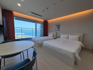Quarto de hotel com duas camas, uma mesa de jantar e vista para o mar.