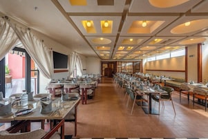 Um restaurante espaçoso com várias mesas e cadeiras, um balcão comprido e vista para o exterior.