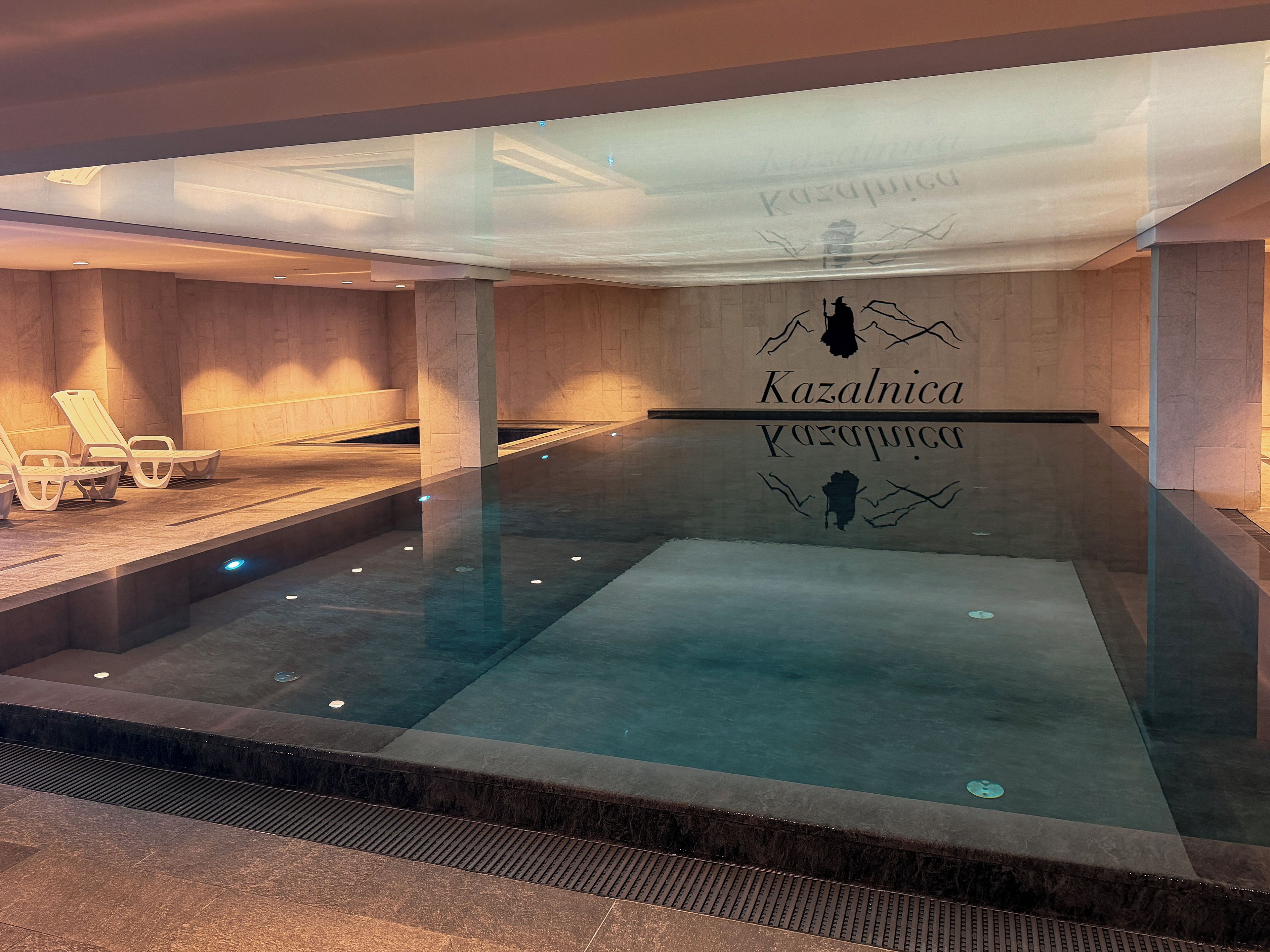 Área da piscina com espreguiçadeiras e uma parede com o nome 'Kazahica'.