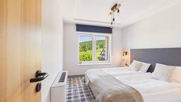 Quarto com cama, janela com vista para áreas verdes, ventilador de teto e abajur.