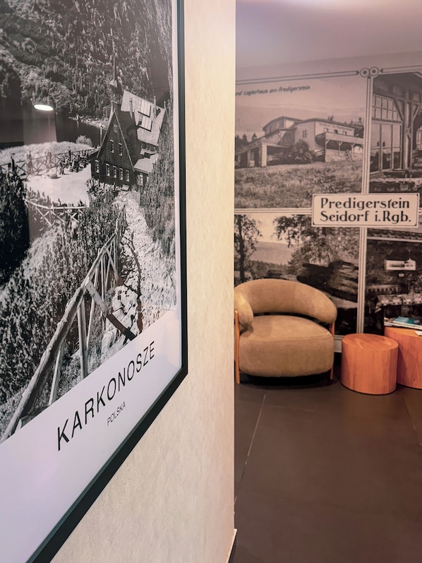 Fotografia antiga emoldurada mostrando uma cena de vila, com uma placa com a inscrição 'KARKONOSZE POLSKA' e uma cadeira em primeiro plano.