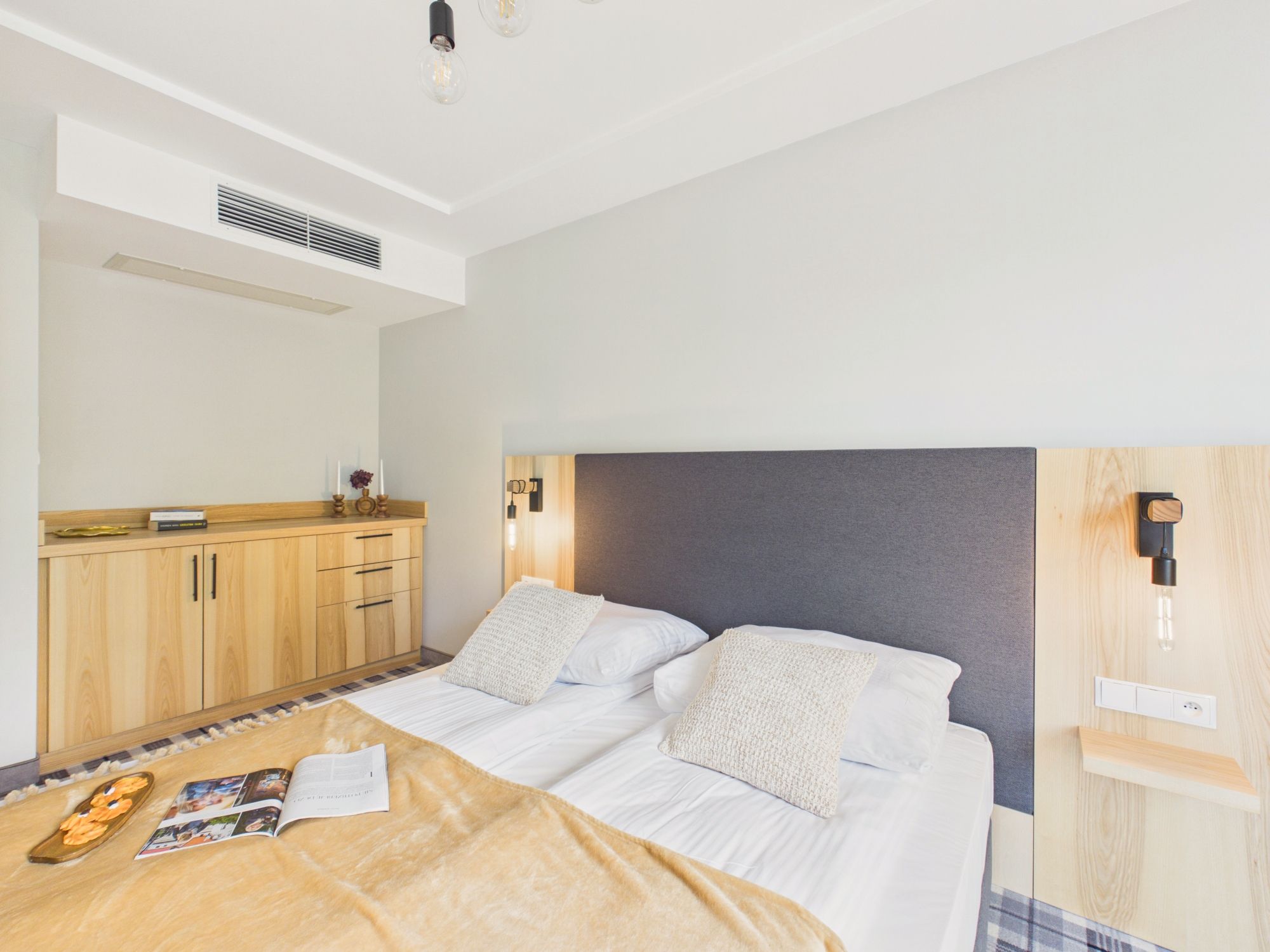 Quarto de hotel moderno com cama, guarda-roupa de madeira e uma mesinha com uma revista.