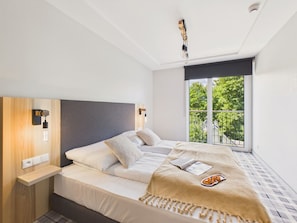 Quarto moderno com cama grande, luminárias de cabeceira, mesa de cabeceira e vista para área verde pela janela.