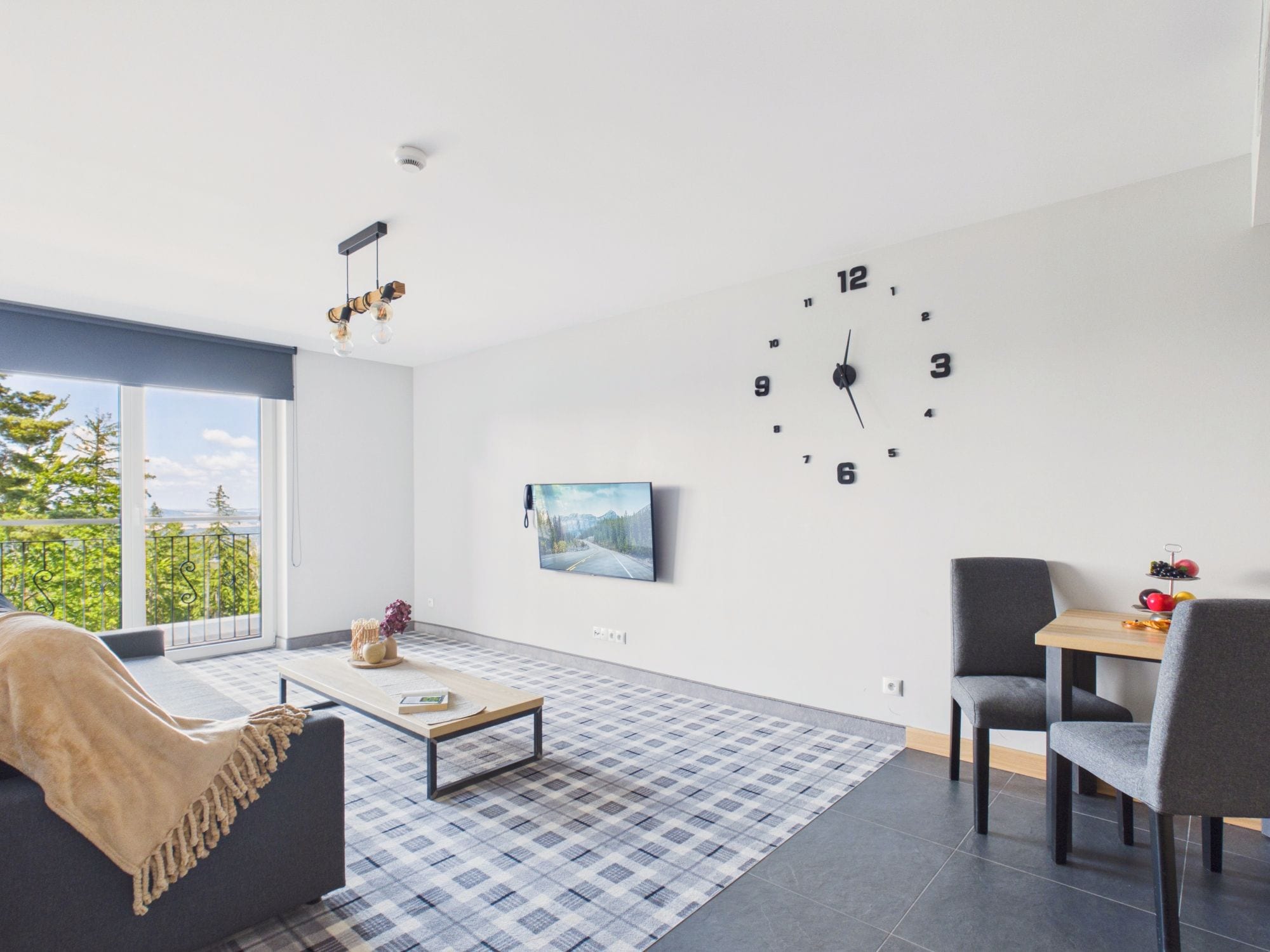 Uma sala de estar moderna com um relógio de parede grande, uma TV de tela plana e um espaço de jantar com mesa e cadeiras.
