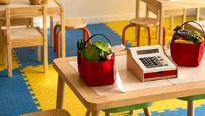 Uma sala de aula com mobiliário de madeira, uma calculadora e cestos com plantas.