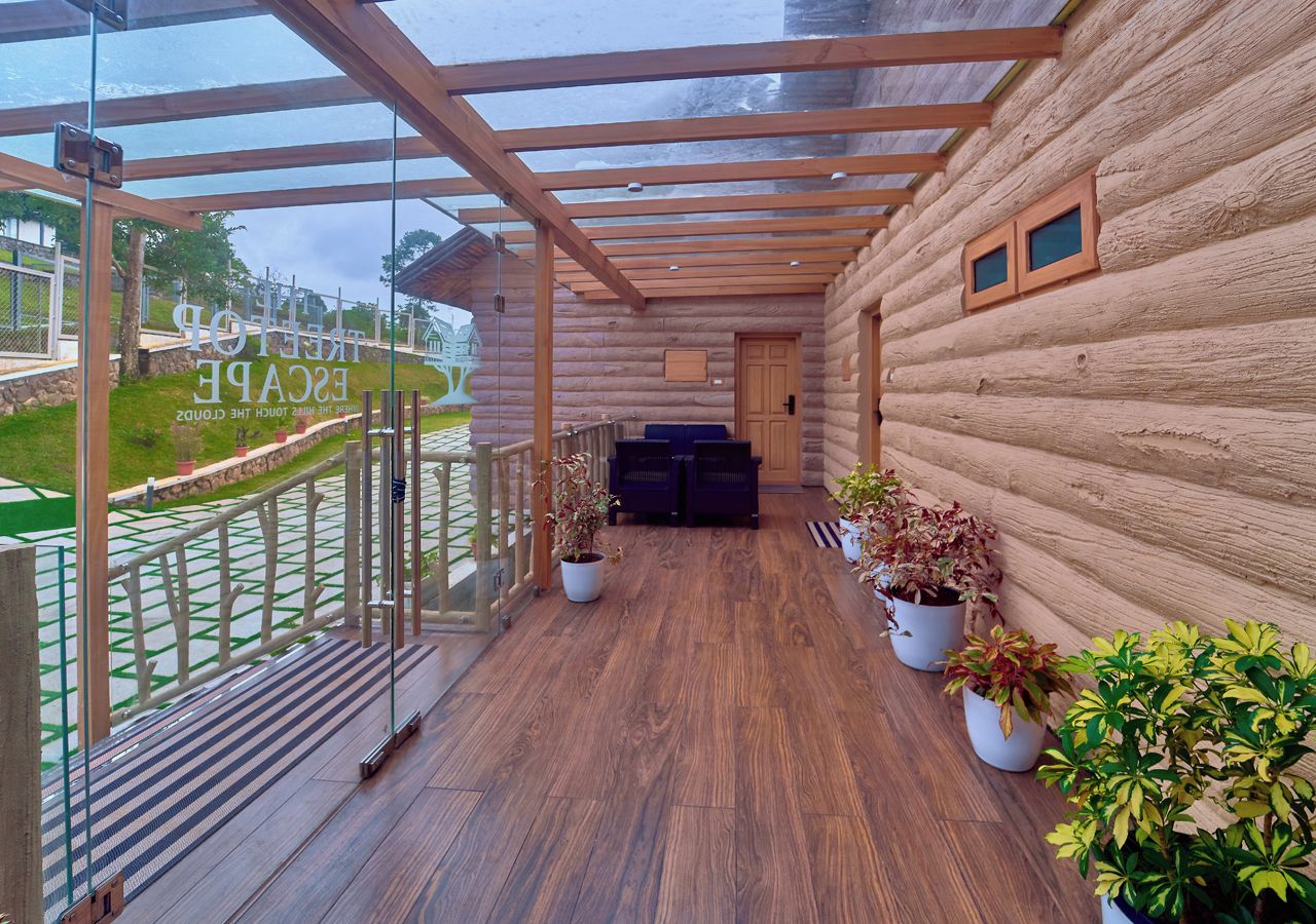 Uma cabana de toras com um deck de madeira, plantas em vasos e guarda-corpo de vidro com vista para uma paisagem verde.
