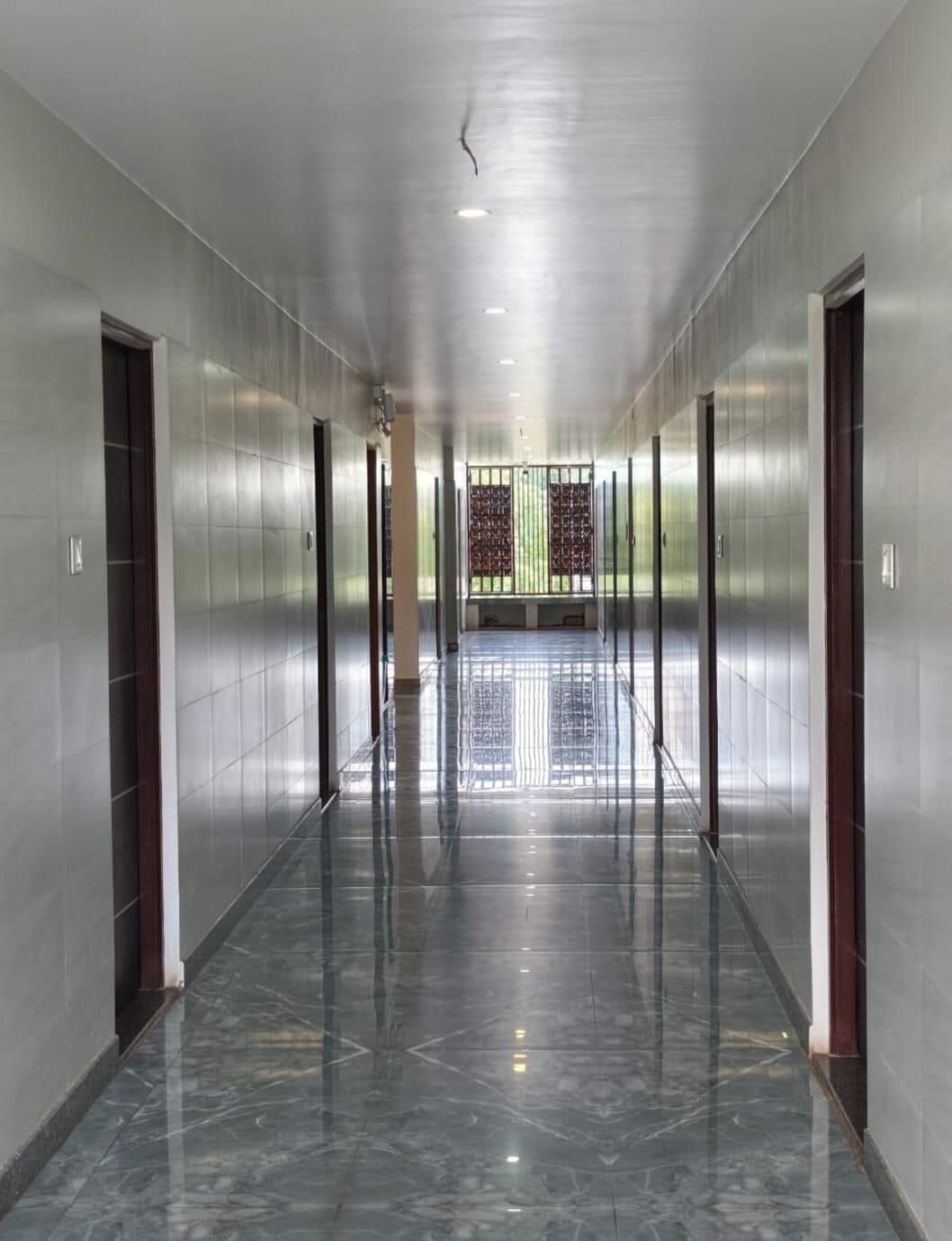 Um corredor com chão de mármore brilhante, paredes metálicas e portas de acesso a elevadores.