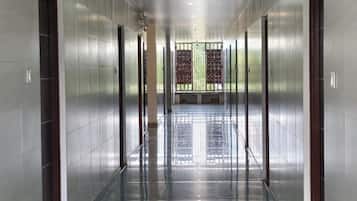 Um corredor com chão de mármore brilhante, paredes metálicas e portas de acesso a elevadores.