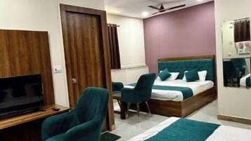 Quarto de hotel com uma cama, duas cadeiras, uma escrivaninha, televisão e ventoinha no teto.