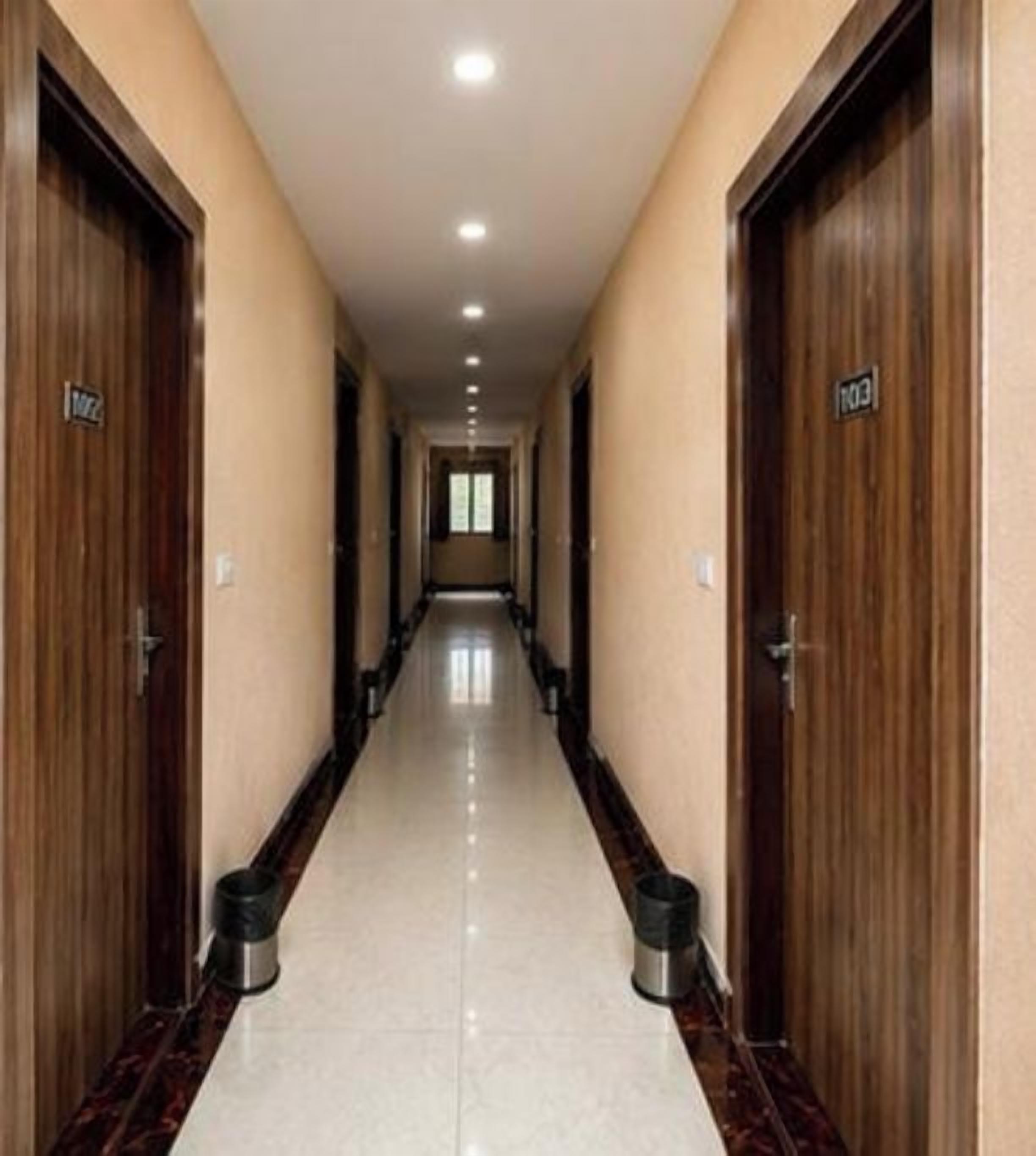 Corredor de hotel com portas de madeira, placas de número de quarto e piso ladrilhado.