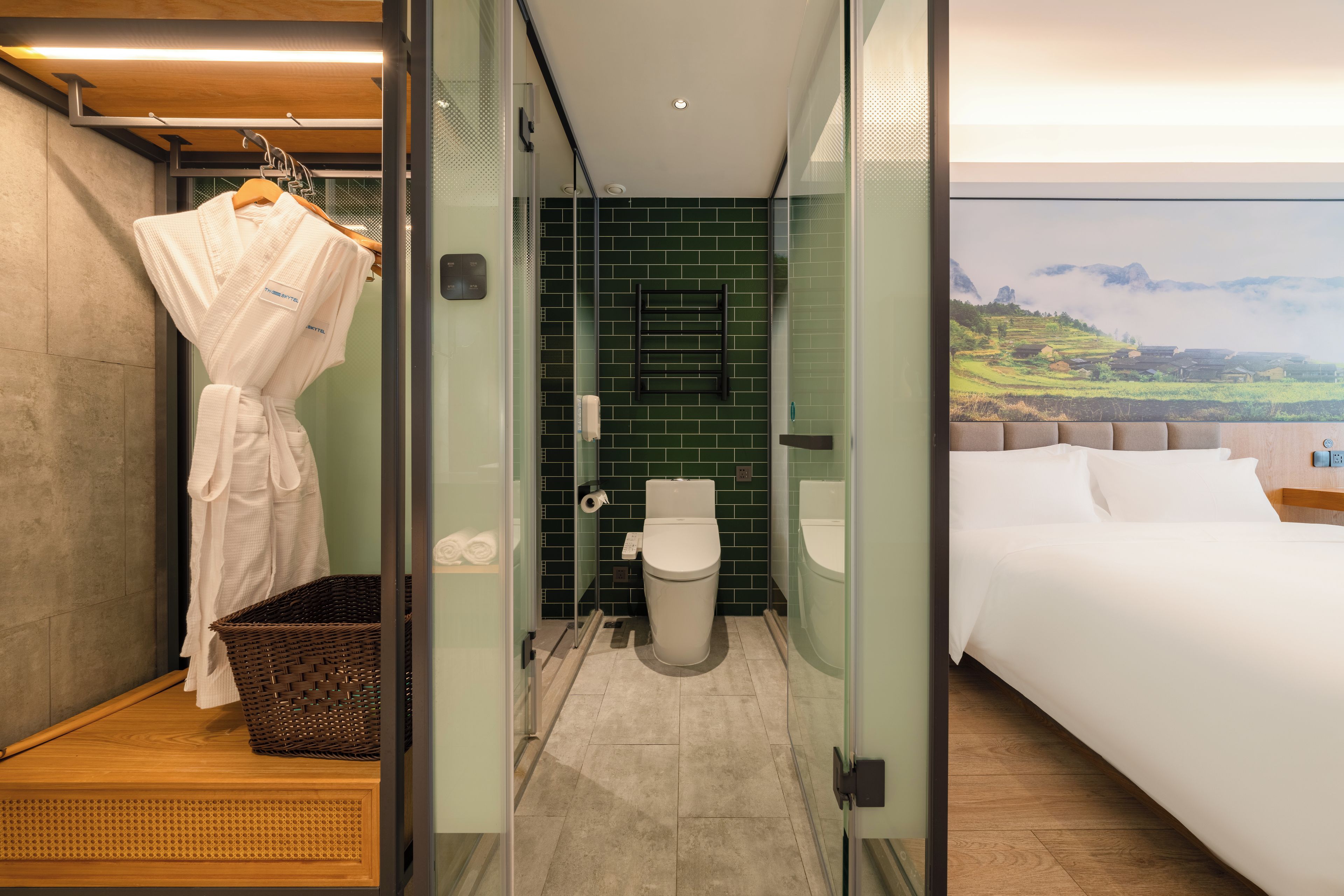 Quarto de hotel moderno com box de vidro, cama branca e vista para uma paisagem montanhosa.