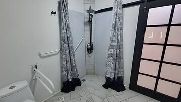 Um banheiro com vaso sanitário branco, chuveiro com cortinas pretas e uma janela grande com moldura preta.