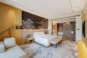 Quarto de hotel moderno com uma cama grande, mesa de cabeceira, abajur, sofá e um mural decorativo na parede.