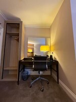 Quarto de hotel com escrivaninha, cadeira e um cesto de lixo pequeno.