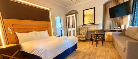 Quarto de hotel com uma cama grande, uma escrivaninha, uma cadeira, um sofá e uma televisão.