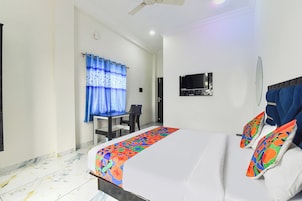 Quarto de hotel com cama, escrivaninha, cadeira, televisão e ventoinha no teto.