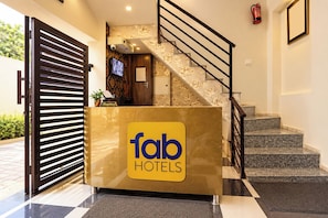 Bancada de recepção com a placa 'fab hotels', escada com corrimão e extintor de incêndio fixado na parede.