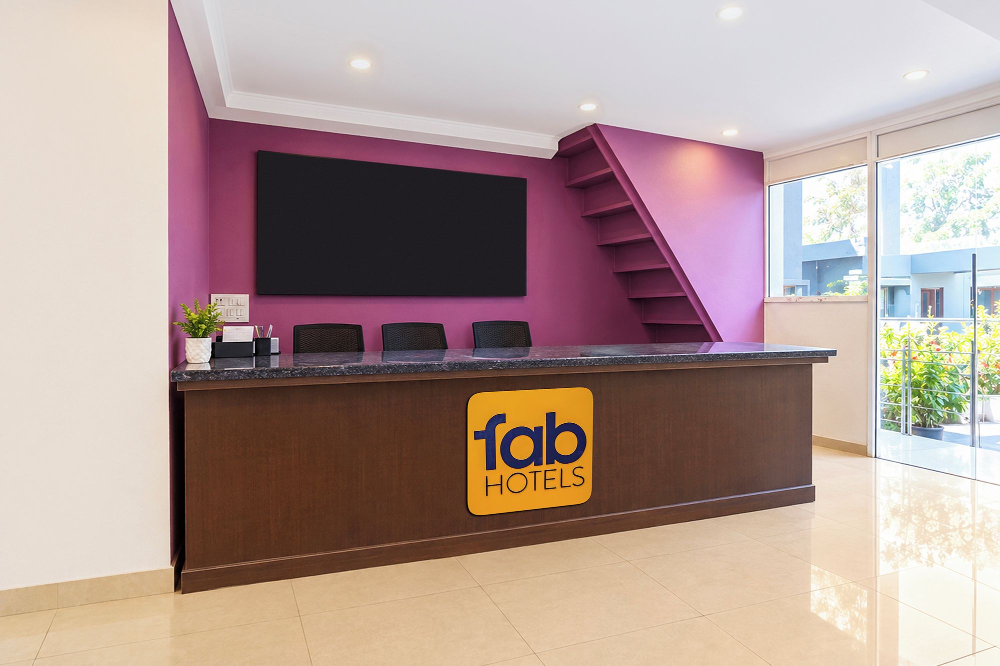 Bancada de recepção com placa 'fab hotels', uma tela preta e uma escada.