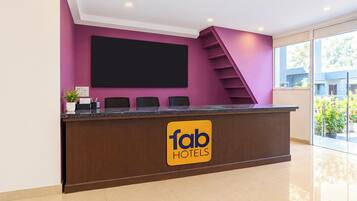 Bancada de recepção com placa 'fab hotels', uma tela preta e uma escada.