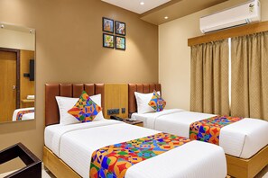 Quarto de hotel com duas camas, cabeceira de madeira, televisão de tela plana e ar condicionado.