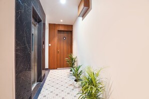 Um corredor com parede de mármore, porta de madeira e plantas em vasos.